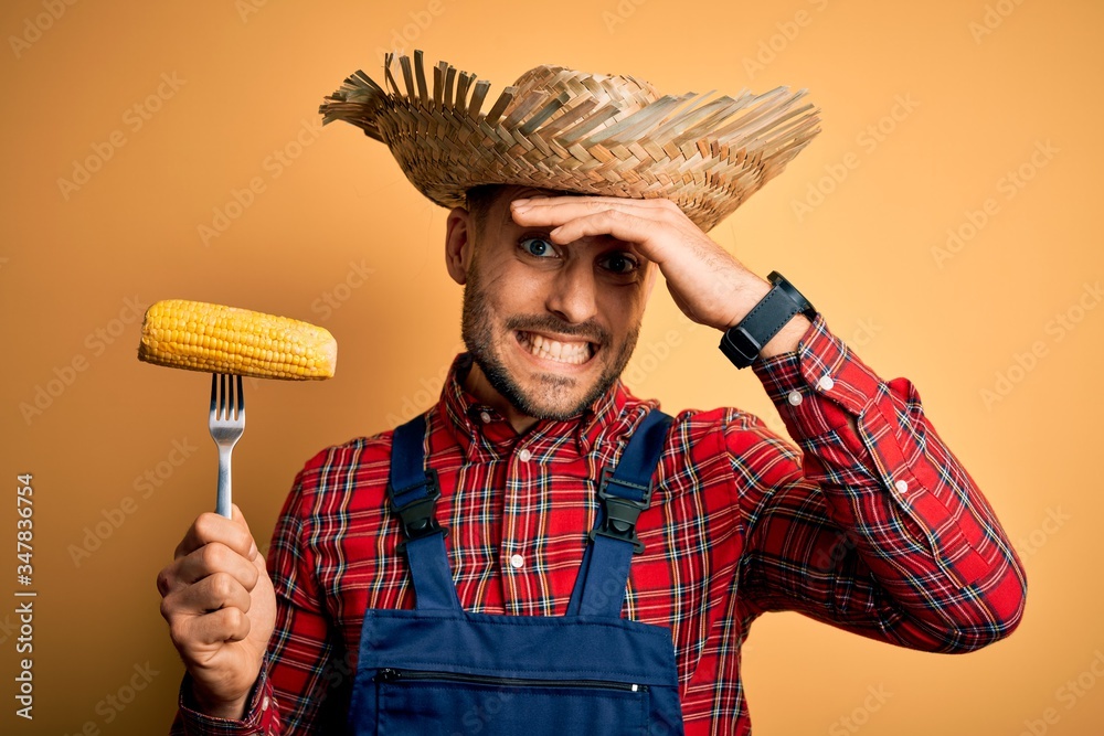 Young rural farmer man holding countryside corn over isolated yellow ...