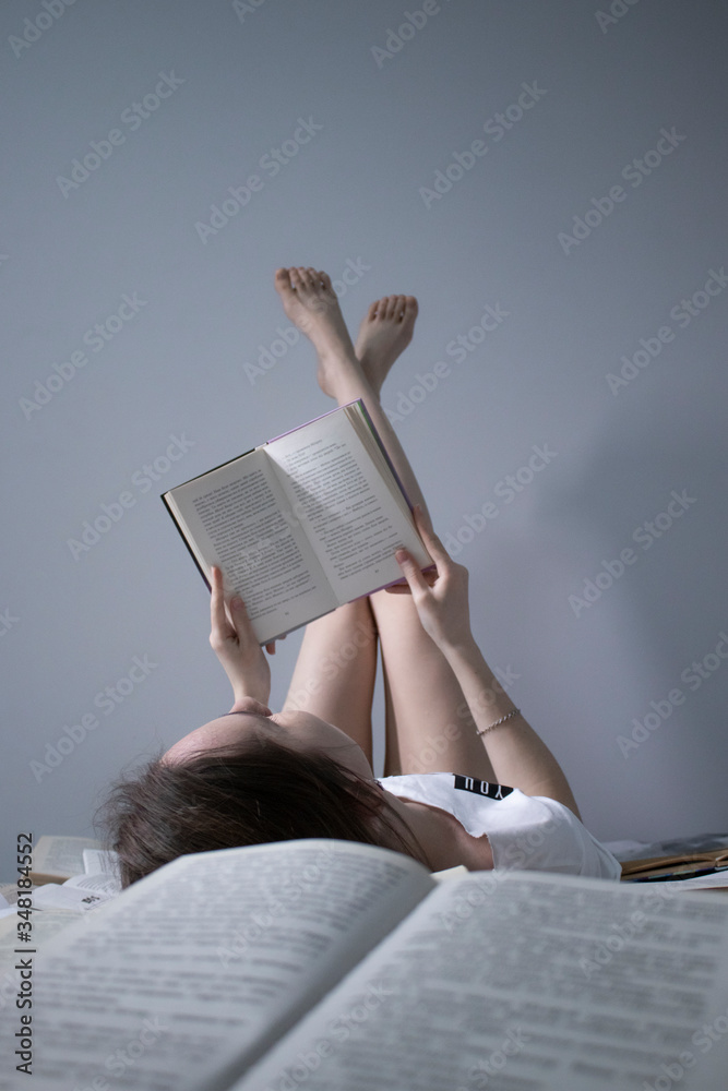 happy beautiful slim girl reading a book lying on the bed full of books ...