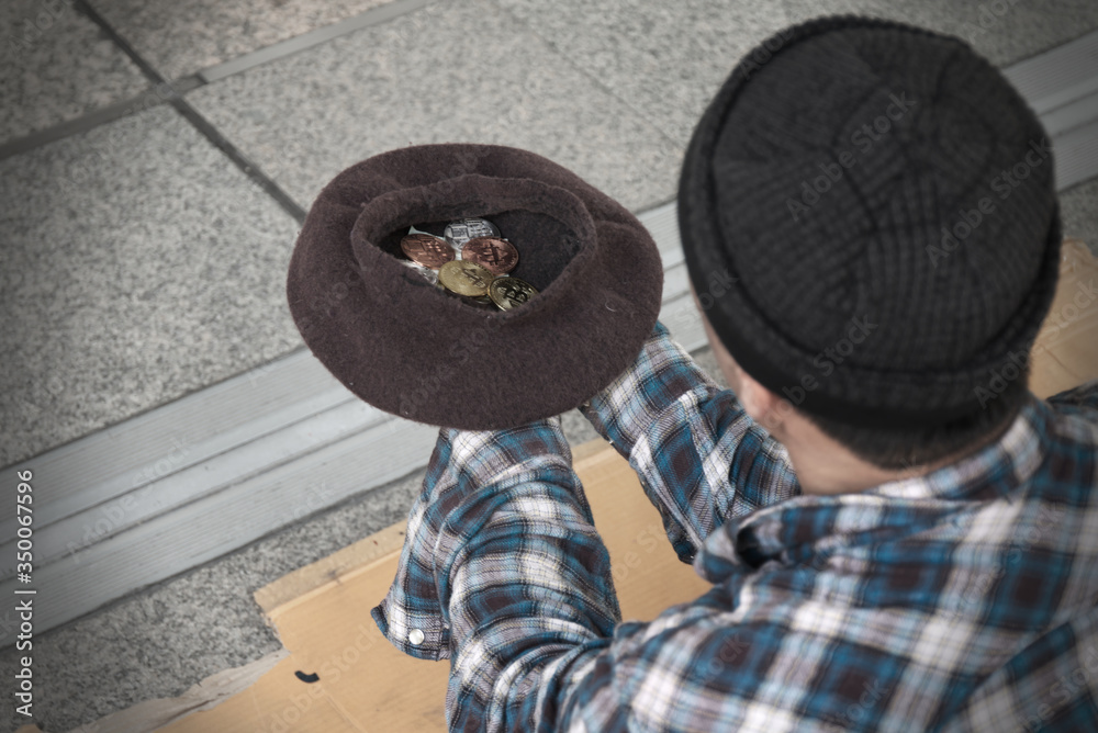 Homeless man sitting on the street in the shadow of the building. He ...