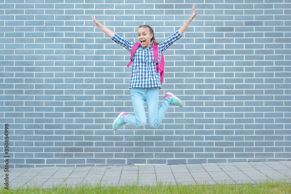 Happy schoolchild with backpack jumping against a brick wall outdoors ...