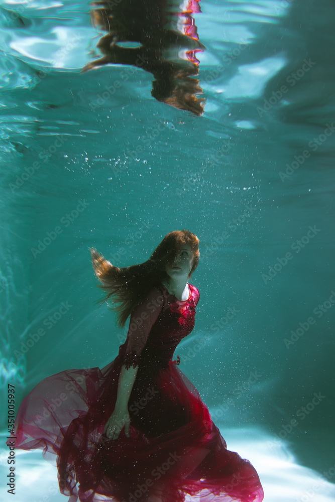 Beautiful girl underwater in a red dress swims in the pool. Tenderness ...
