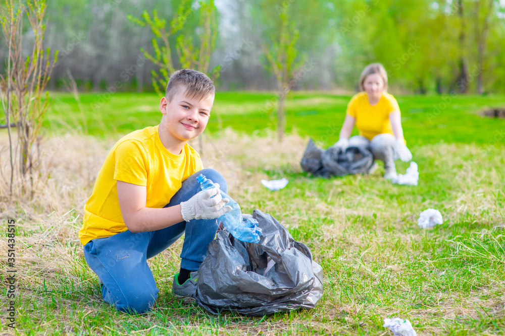 Smiling boy picking up trash in the park with his mother. Volunteer and ...