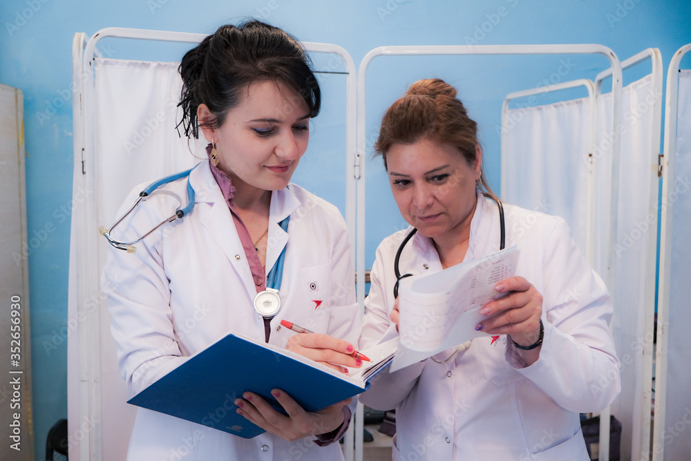 two women doctors look at patient tests,looking through some patients ...