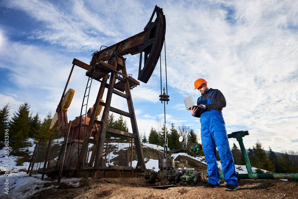Male worker using notebook controlling work of petroleum pump jack ...