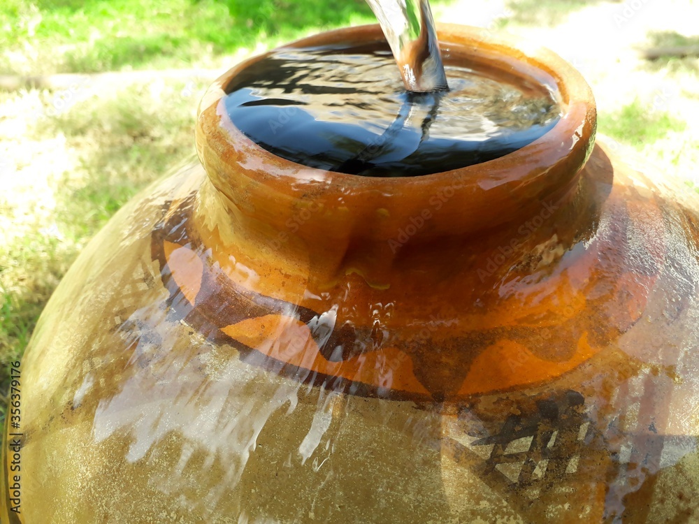 Filling water in a clay pot overflowing in summer during lack of water ...