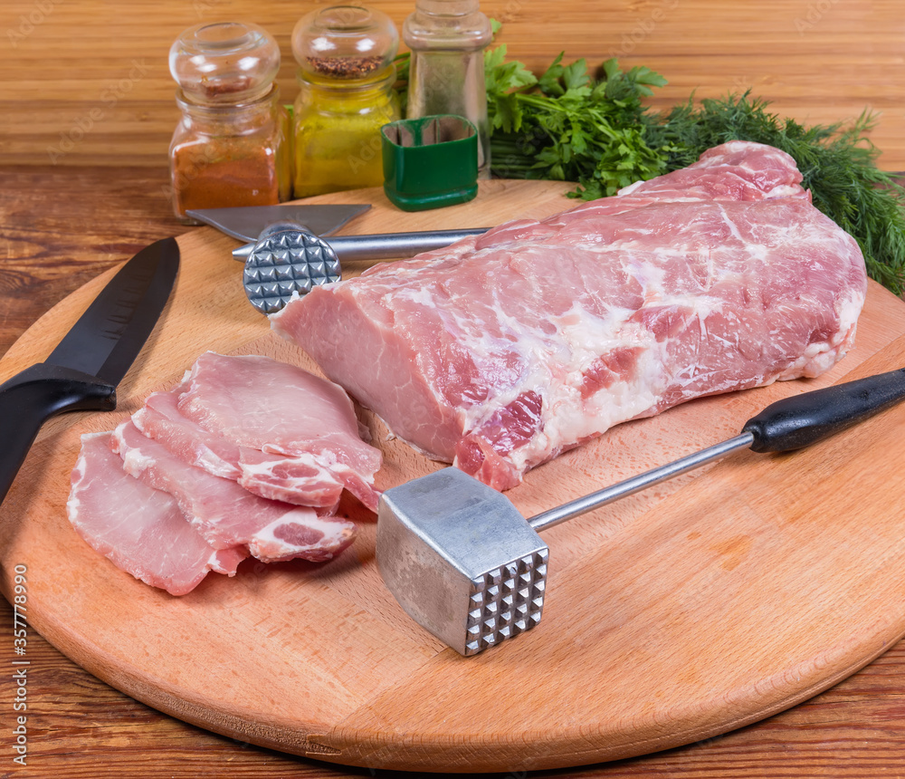 Partly sliced uncooked pork loin, kitchen utensils, spices and greens ...