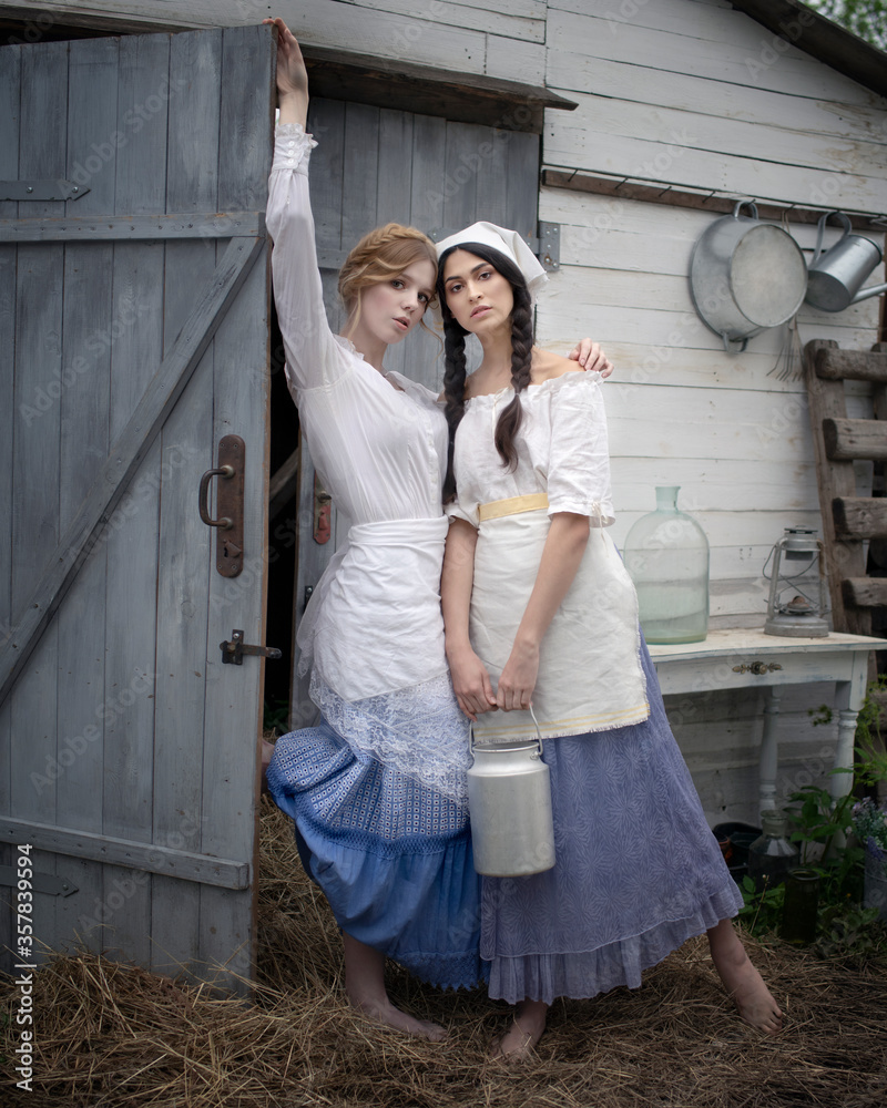 Art photo of two maiden girls at a farmhouse with a can and hay Stock ...
