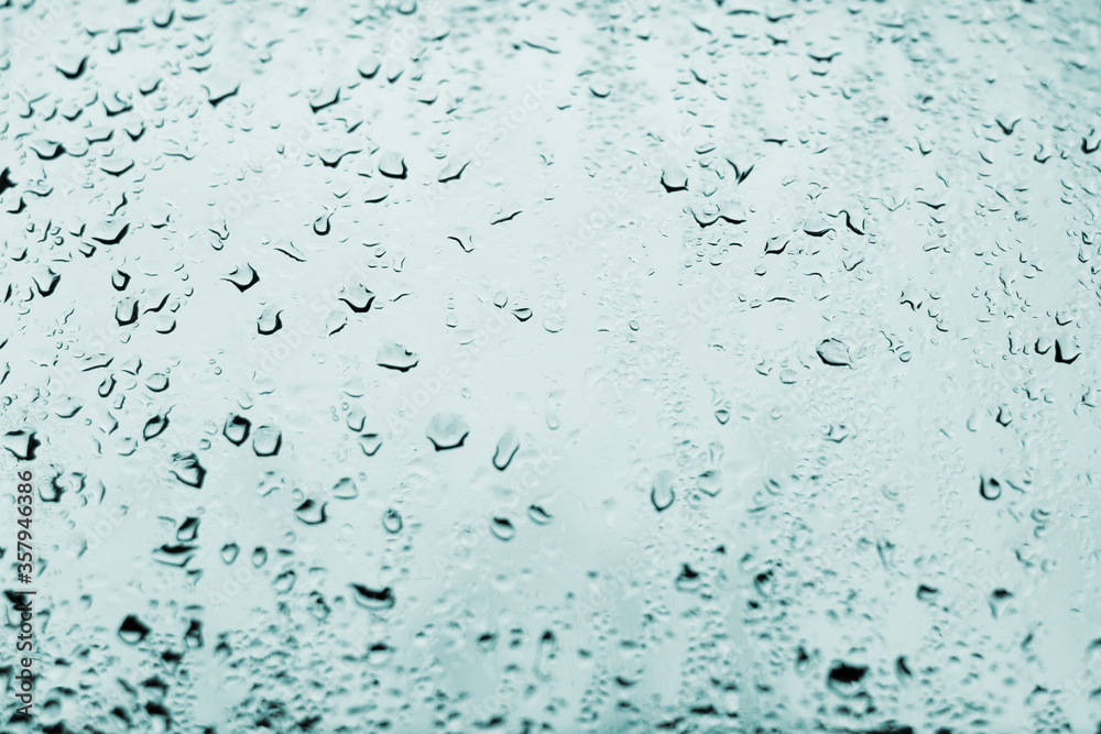 High contrast photo of drops of rain on a window glass with light cyan ...