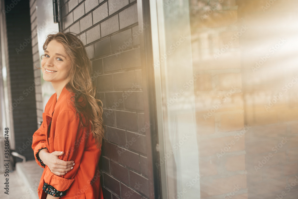 Lovely cheerful young woman lean to wall and posing on camera. Sun ...