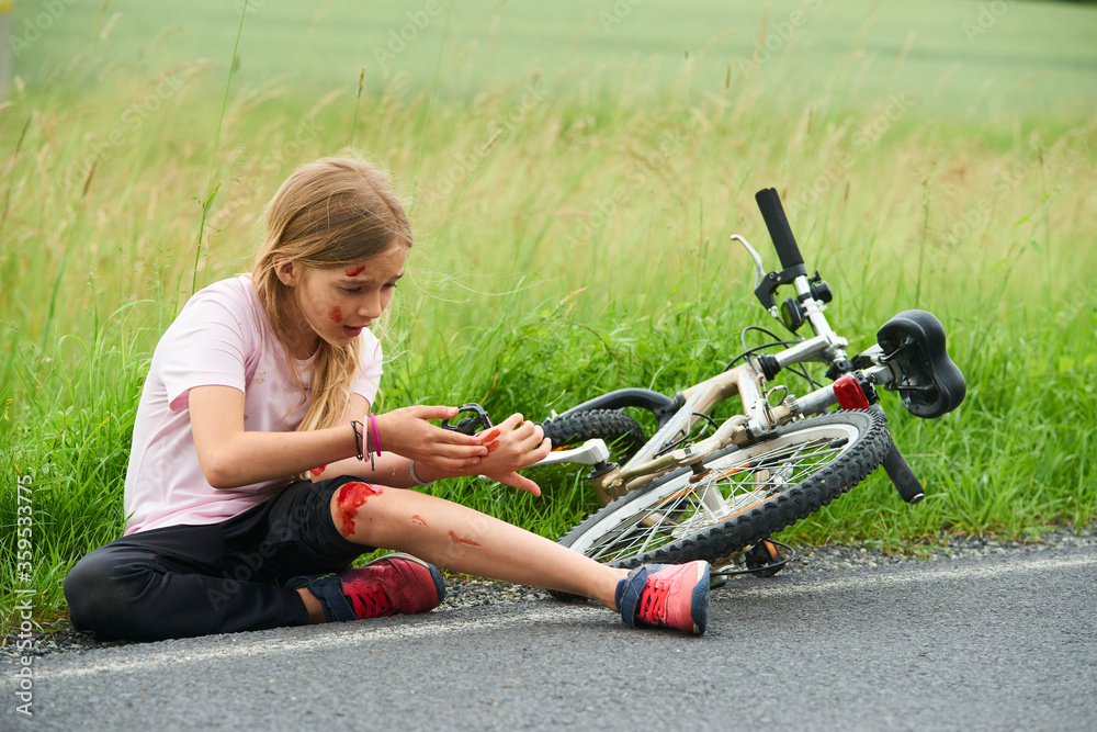 Sad crying little child girl fell from the bike in the summer park ...