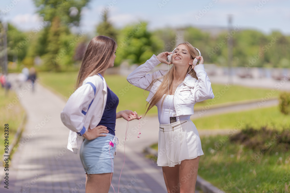 Two blonde girls with long hair in short shorts are walking in the park ...