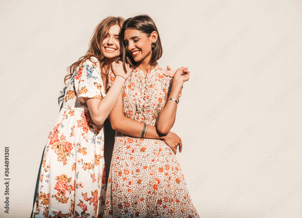 Two young beautiful smiling hipster girls in trendy summer sundress ...