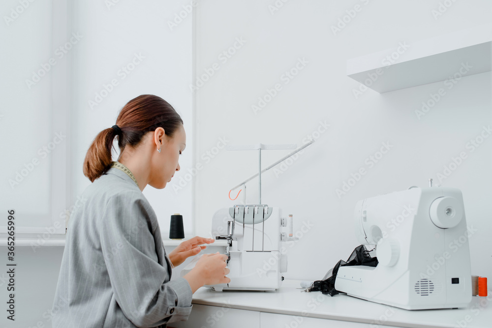 Female tailor with a centimeter ribbon over the neck is adjusting the ...