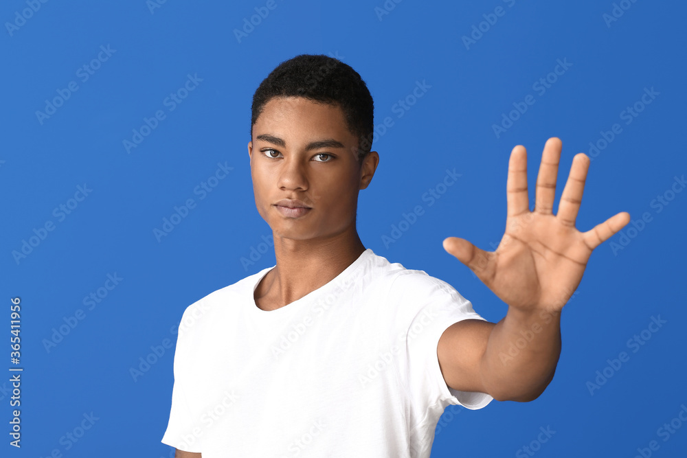 Sad African-American teenage boy showing stop gesture on color ...