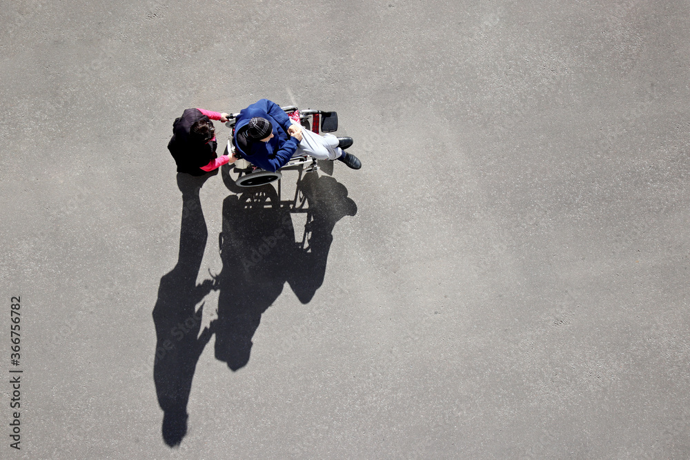 Woman carries a disabled person in a wheelchair on a city street, top ...