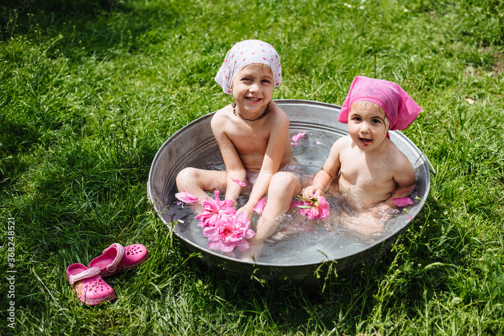 Happy children take a bath in the garden, with peony flowers. Two ...