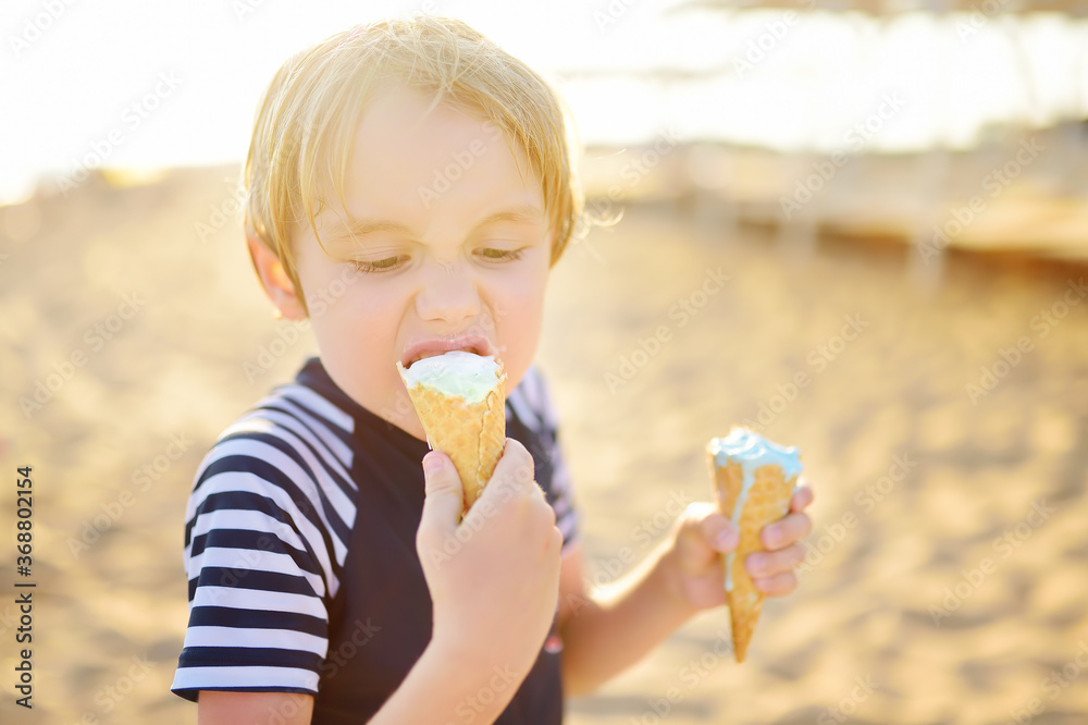 Preschooler boy eating ice cream on hot summer day on beach during ...
