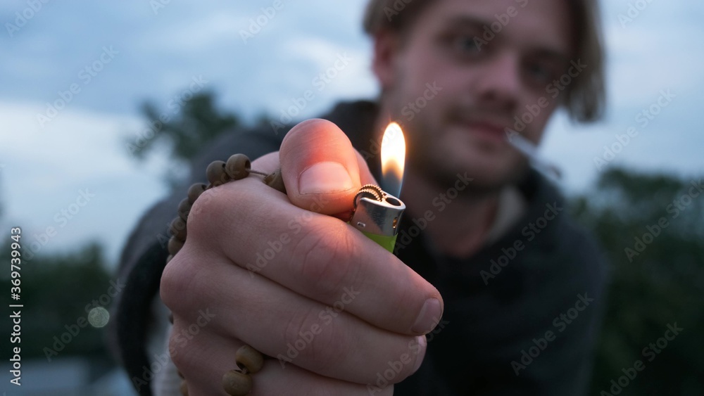 Man on the street lights lighter rack focus. The guy brings lighter to ...