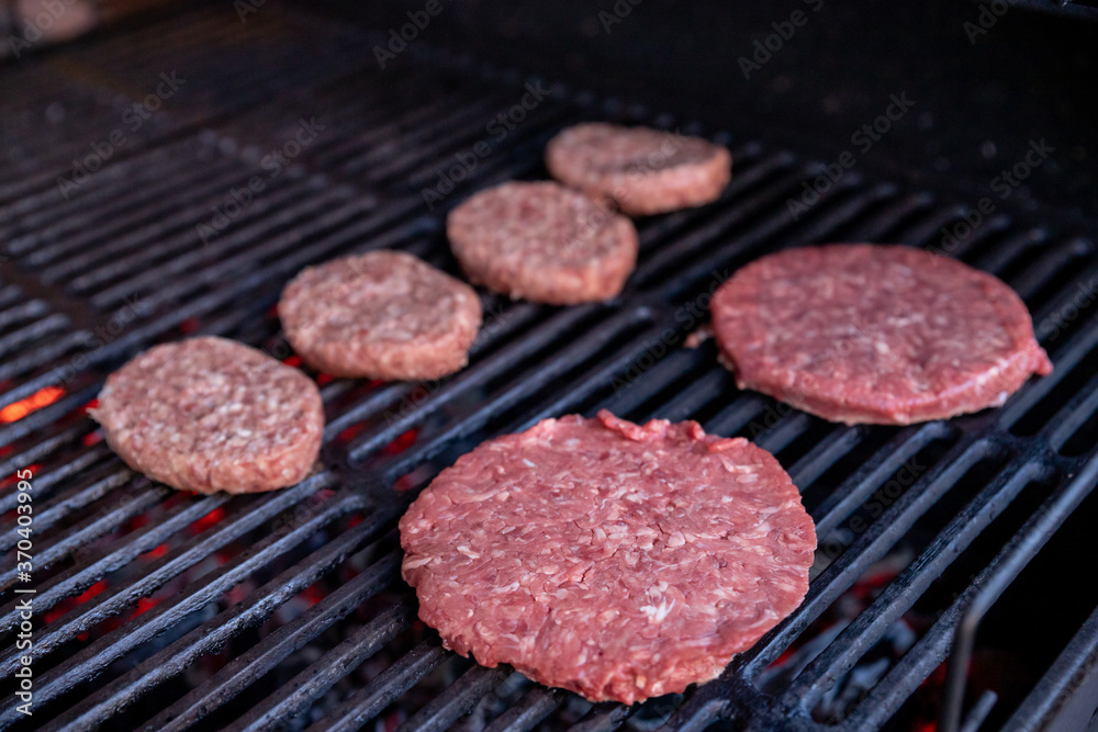 Raw beef burgers with a pinch of salt and black pepper on grill ...