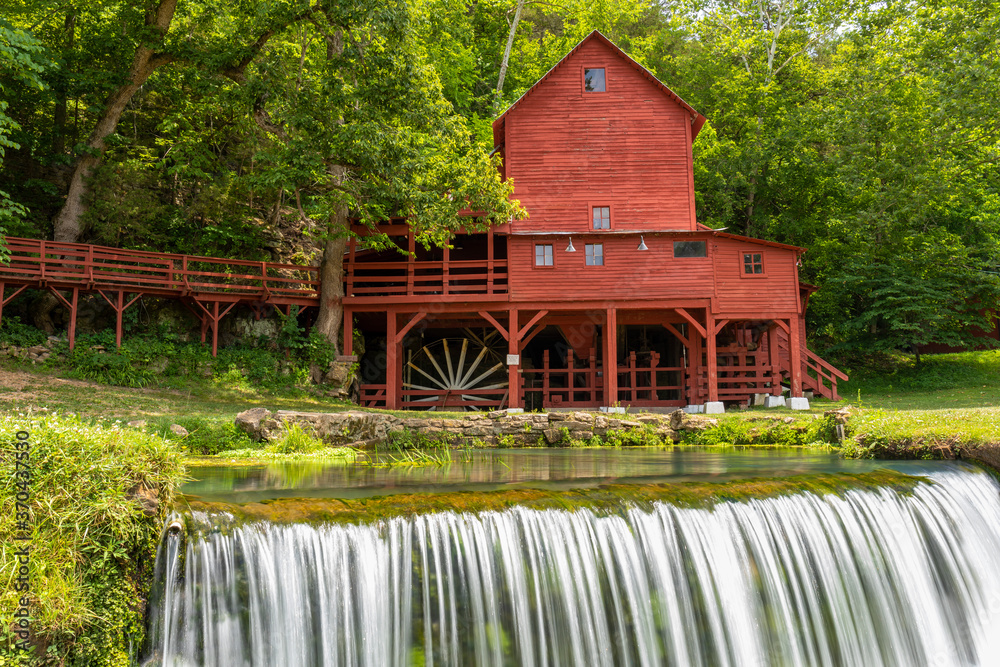 An old red grist mill with a small waterfall. Stock Photo | Adobe Stock