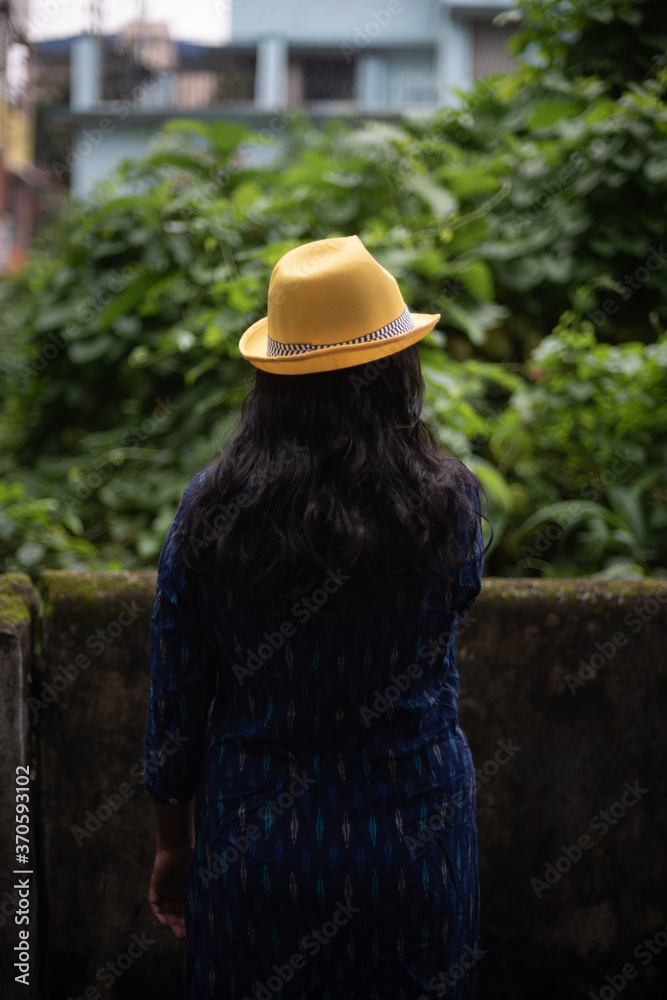 Backside view of an Indian woman standing in front of a green bush ...