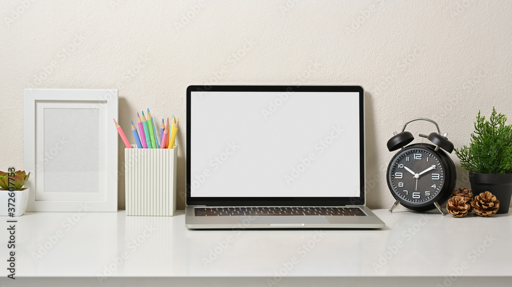 Stylish workspace with laptop, frame pictures, clock, coloured pencil ...