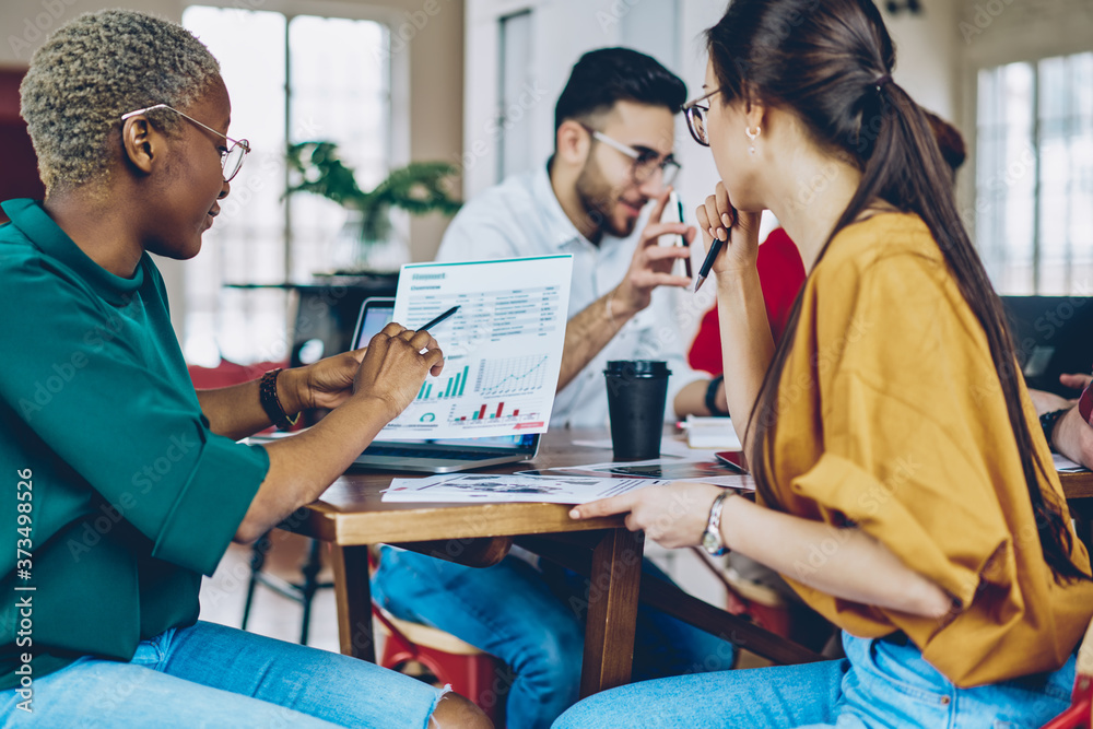 Multiracial female colleagues analyzing graph charts with financial ...