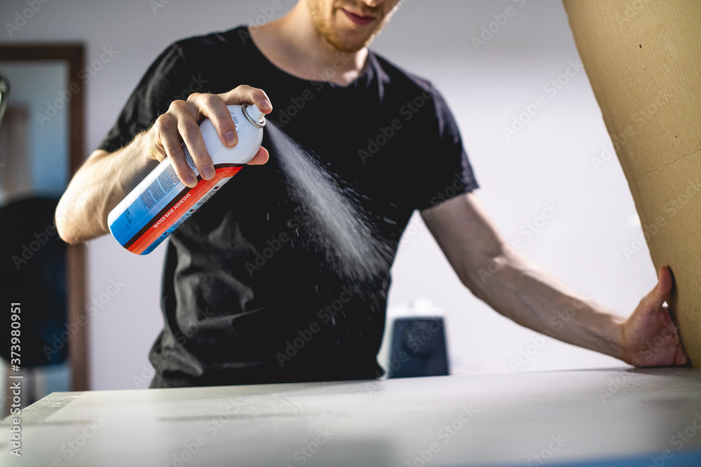 Cropped view of craftsman spraying tack glue on surface while working ...