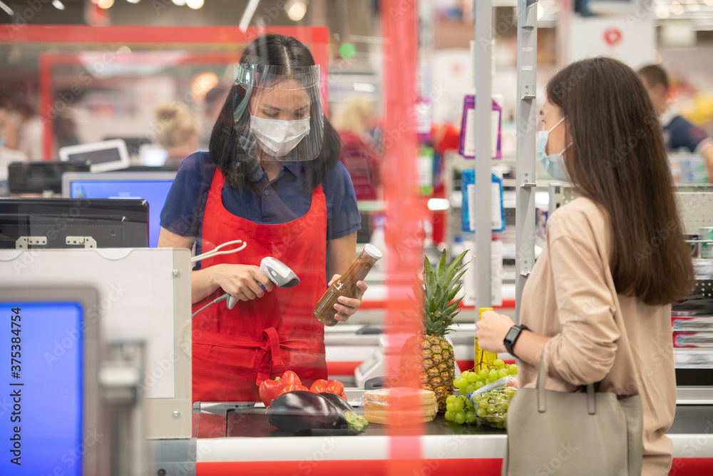 Stock-Foto „Young cashier wearing mask on face checkingout foods for ...