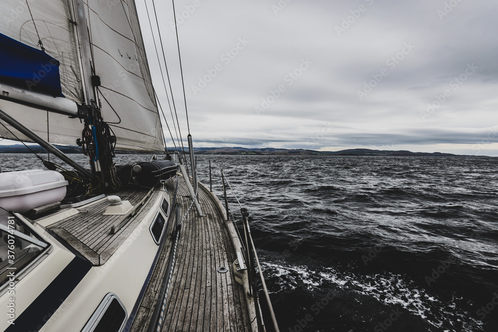 Sloop rigged modern yacht with wooden teak deck sailing near the rocky ...