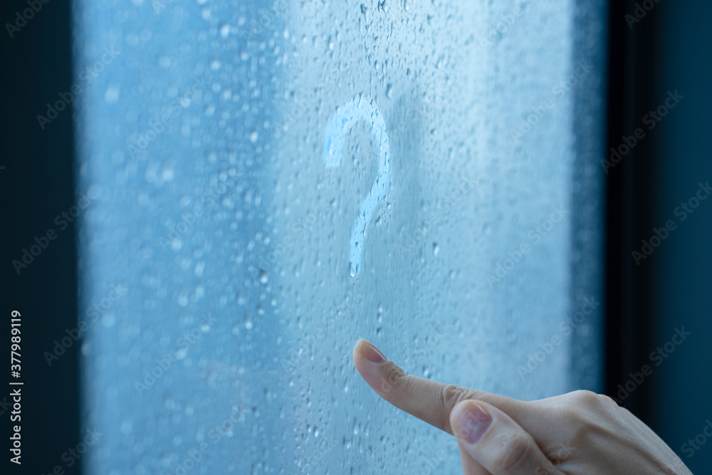 Female hand draws a question mark on a foggy window during the rain. A ...