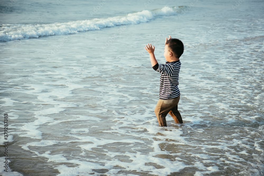 Rearview of little Asian child walking on the tropical beach. Boy ...