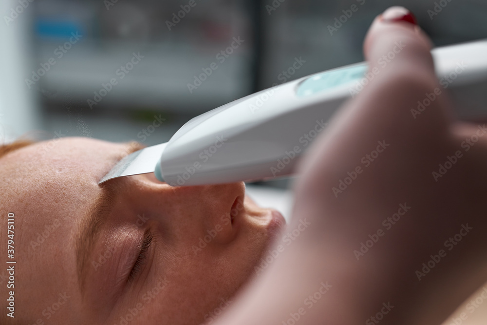young female on procedure of ultrasonic cleaning of face, ultrasonic ...