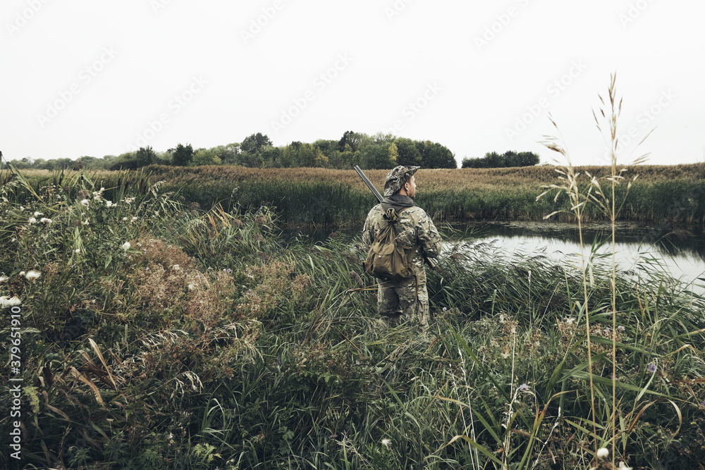Disguise and camouflage. Hunter with a gun in the thick grass. Opening ...