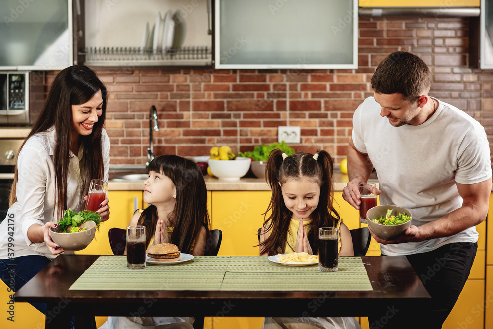 Healthy eating vs bad habits. Parents offer their daughters a salad ...