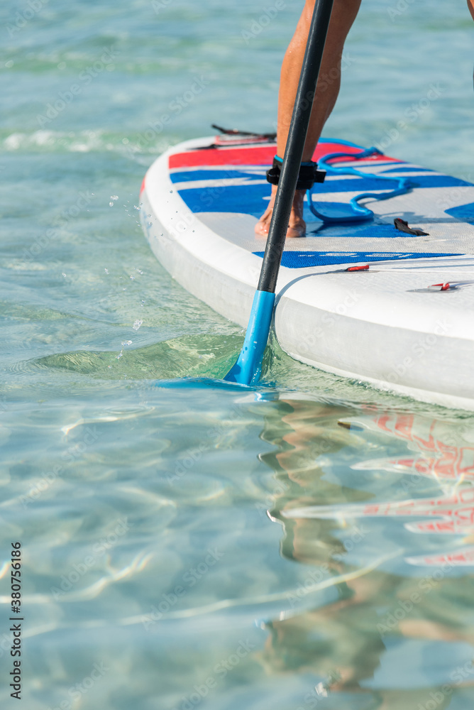 Crop anonymous female surfer standing on surfboard and rowing with ...