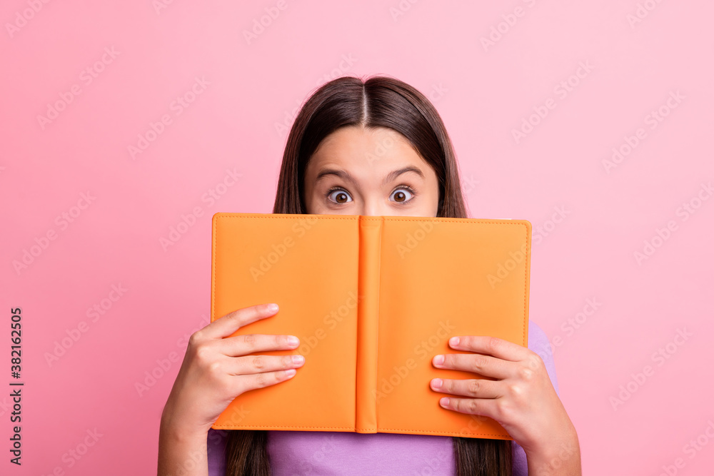 Photo of excited impressed kid girl hide her lips with book wear violet ...