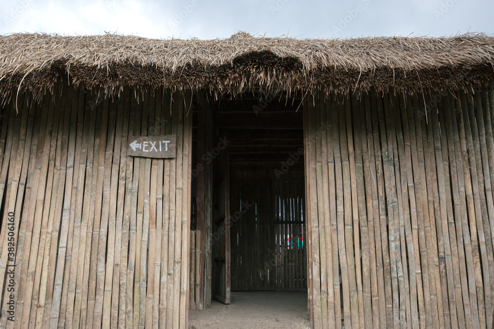 Exit sign by the door of a tropical hut made of thatched dry leaves and ...