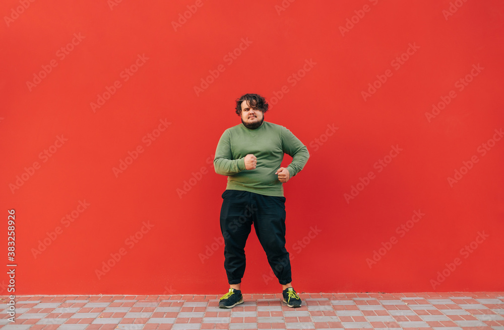 Funny young overweight man dances on a red background and looks away ...