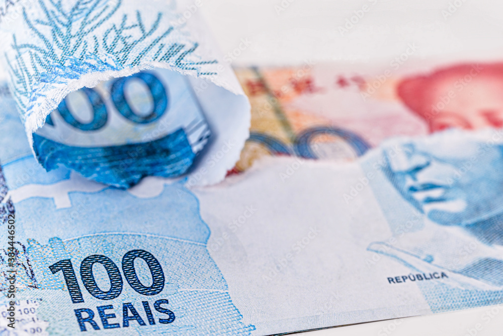 banknote of 100 reais from brazil, torn, revealing a hundred yuan note ...