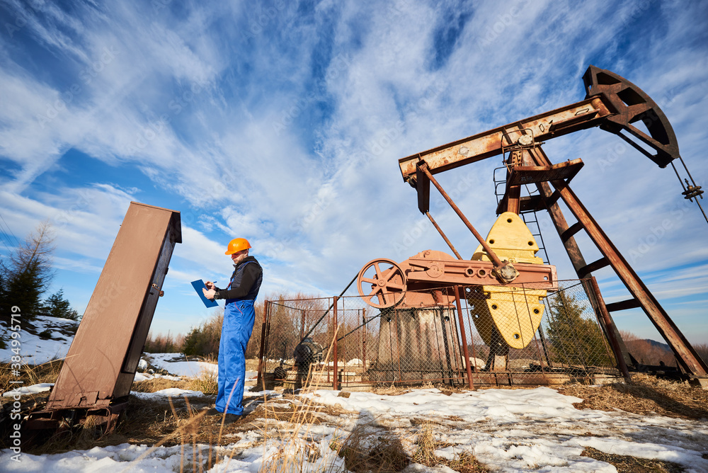 Petroleum engineer in work overalls and helmet making notes on ...