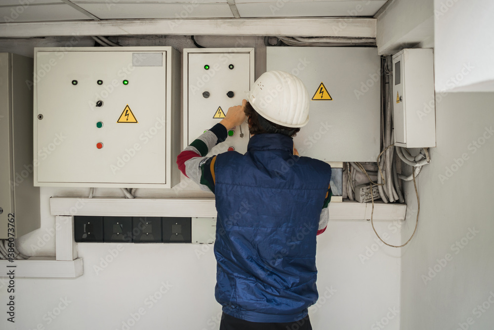 An electrician in an engineering helmet opens the switch box. The ...