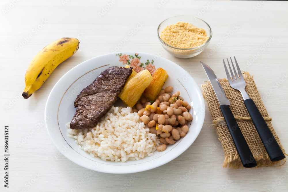 Plate of rice, beans, steak and cassava. With cutlery and manioc flour ...