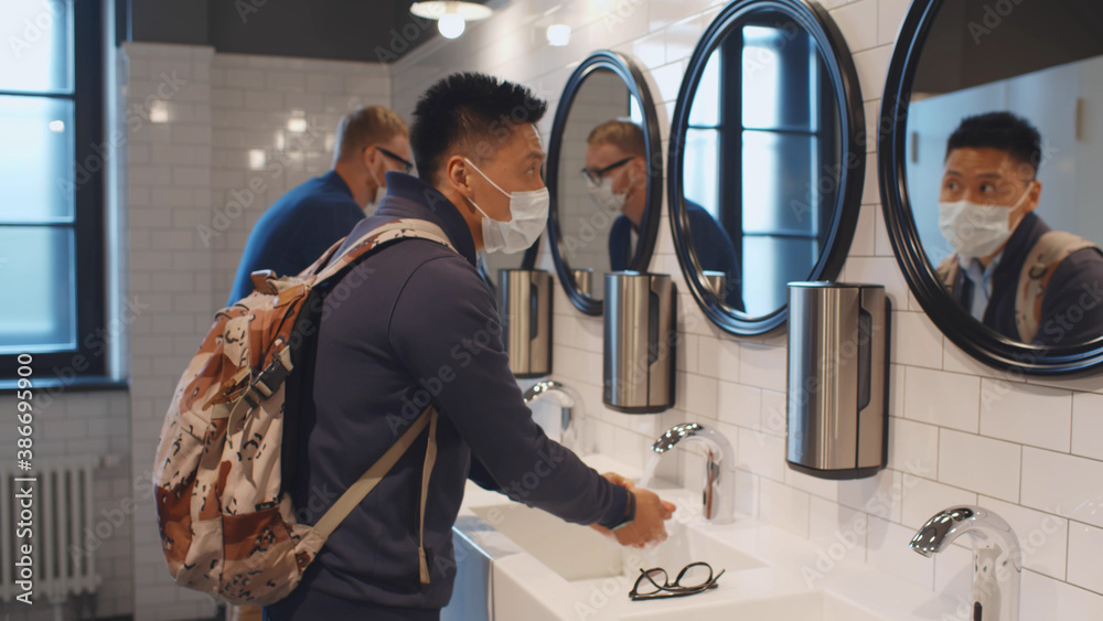 Students in mask visiting restroom in college and washing hands with ...
