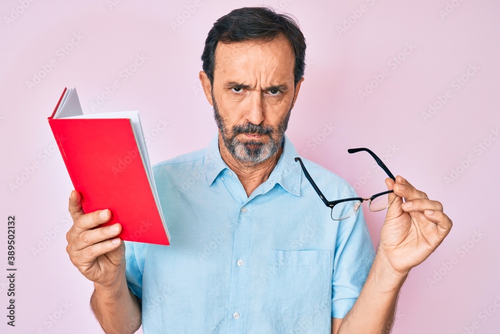 Middle age hispanic man reading book holding glasses skeptic and ...