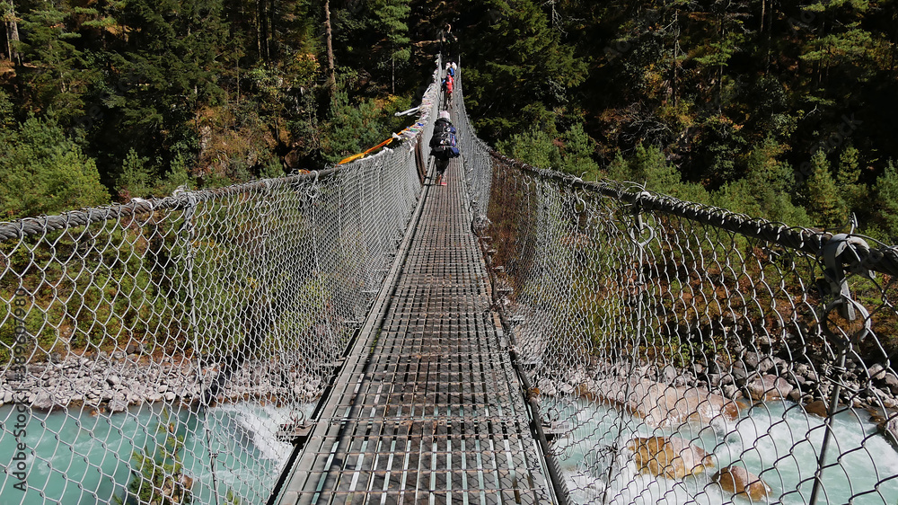 Porters crossing a suspension bridge with attached Buddhist prayer ...