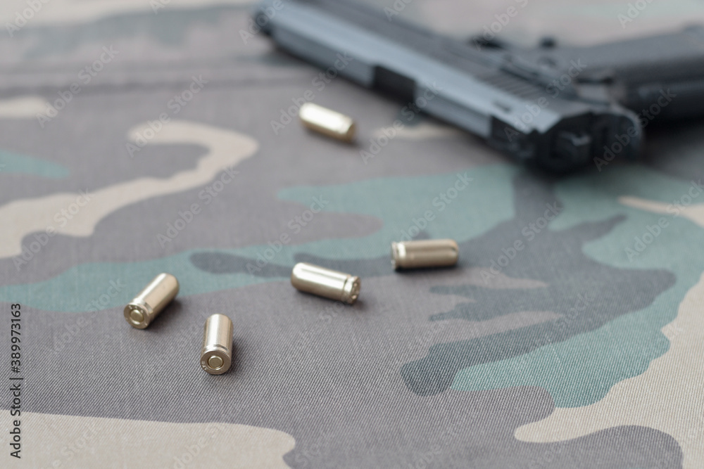 9mm bullets and pistol lie on camouflage green fabric. A set shooting ...