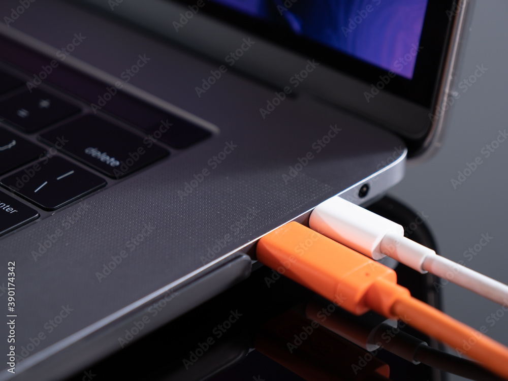 Two USB type C cables connected to laptop computer on black background ...