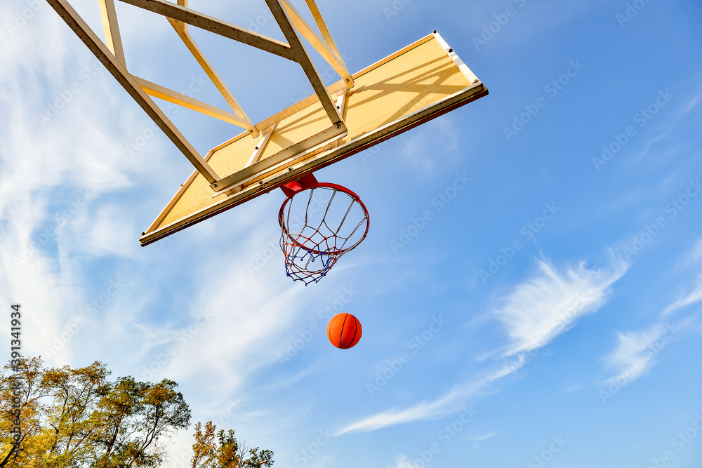 Flying basketball ball in the hoop on the background of the cloudy sky ...