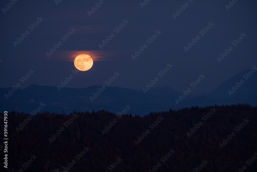 huge orange full moon rising behind a mountain ridge illuminating misty ...